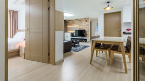 Um apartamento moderno com piso de madeira, área de jantar com mesa e cadeiras, cozinha com televisão e quarto com cama e cortinas.