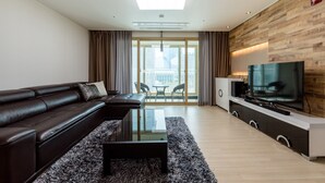 Uma sala de estar moderna com um sofá de couro, uma mesa de centro de vidro, uma televisão de tela plana e uma parede de destaque em madeira.