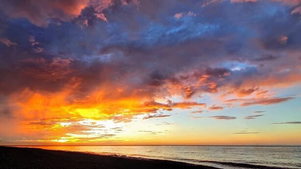 Um pôr do sol sobre uma praia com céu limpo e mar calmo.