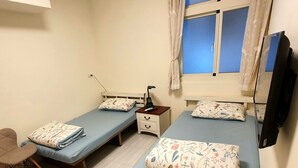 Quarto com duas camas de solteiro, uma escrivaninha, uma cadeira, televisão e janela com cortinas.