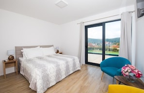 Quarto de hotel com cama, mesa de cabeceira, cadeira e vista para o exterior.
