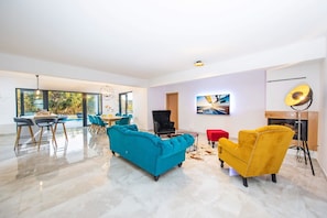 Uma sala de estar espaçosa, com um sofá grande, uma poltrona menor e uma área de jantar com mesa e cadeiras.
