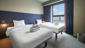 Quarto de hotel com duas camas, uma janela grande com cortinas, uma luminária no teto e uma lixeira.