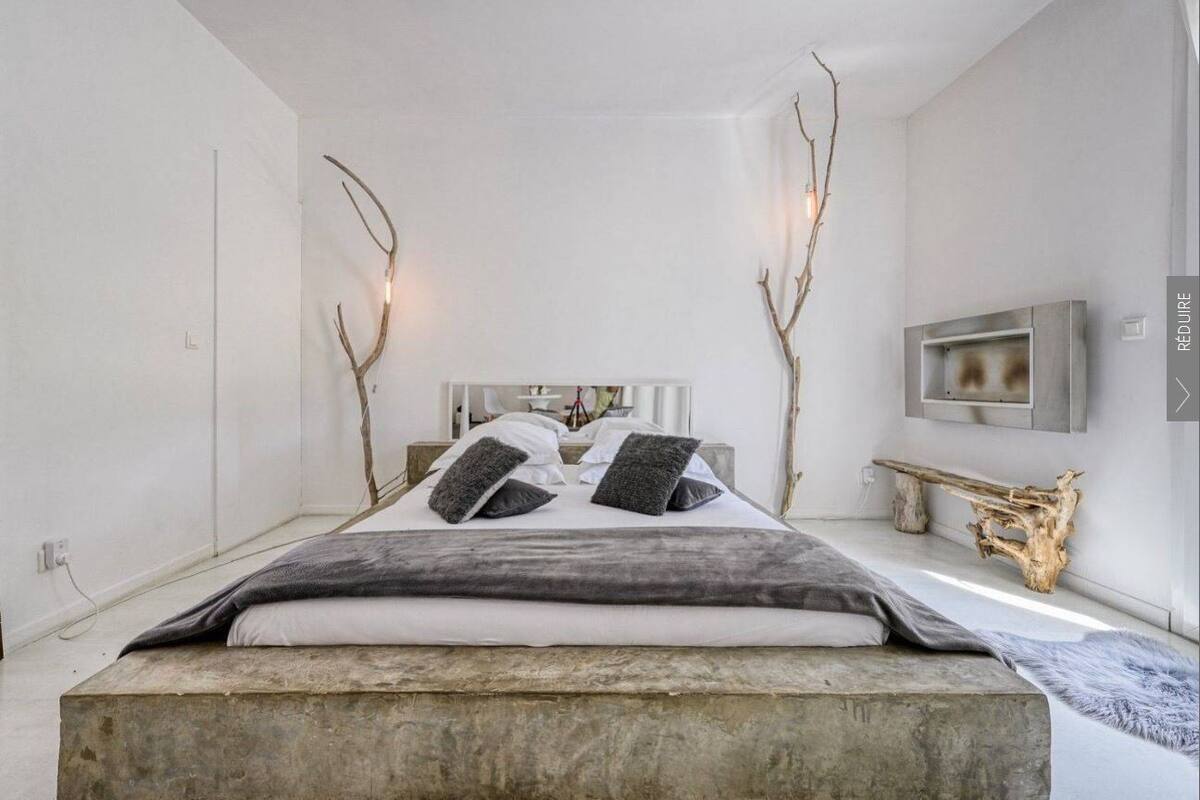 Quarto moderno com uma cama grande, dois galhos decorativos, uma televisão montada e um banco de madeira rústica.