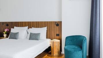 Quarto de hotel moderno com cabeceira de madeira, poltrona verde-água e um banquinho de madeira.