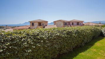 Fileira de edifícios em estilo mediterrâneo tradicional com telhados de terracota, cercada por um conjunto de sebe bem cuidado.