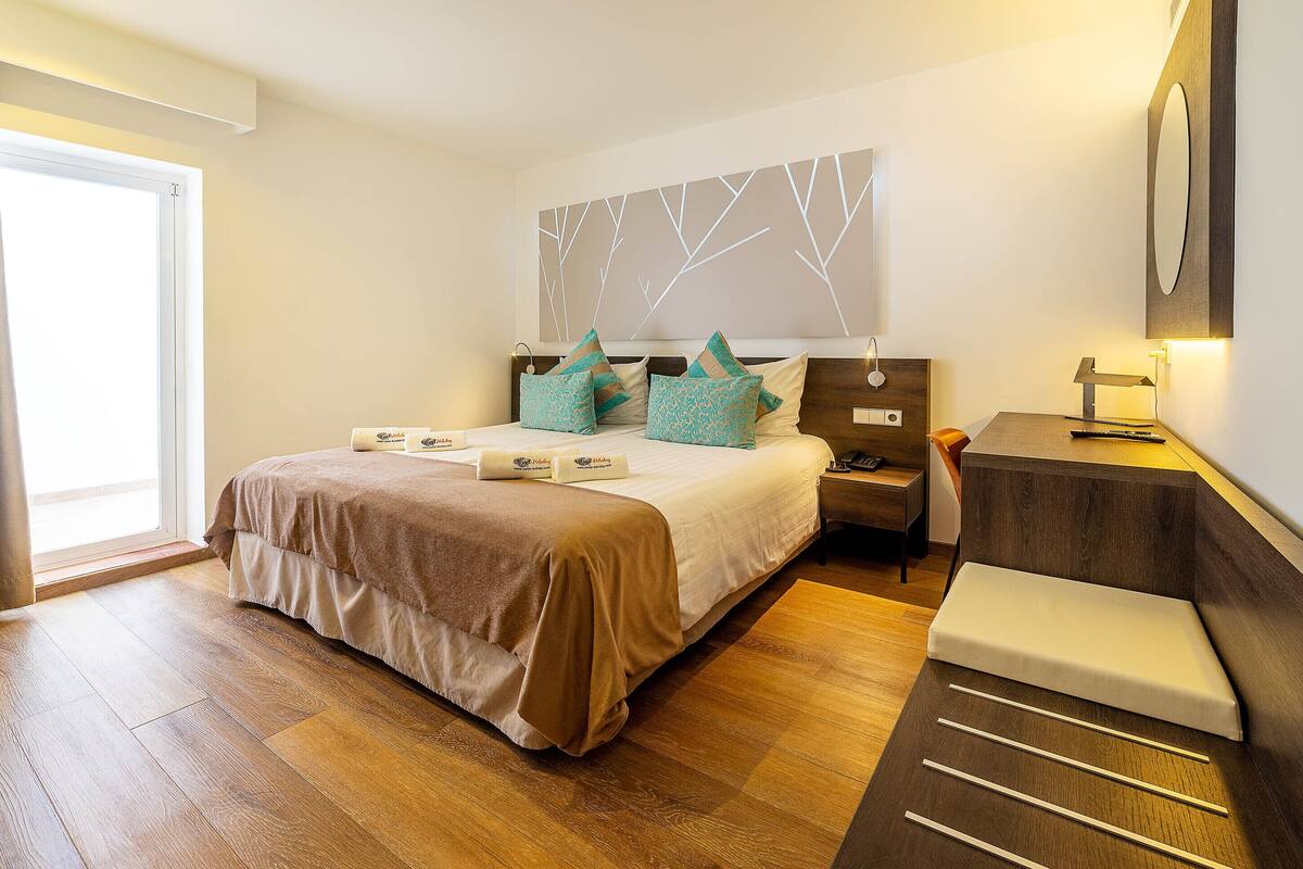 Quarto de hotel com cama, mesa de cabeceira e área de trabalho.