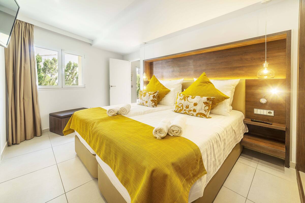 Quarto de hotel com uma cama grande, uma mesa de cabeceira, cortinas e vista para árvores.