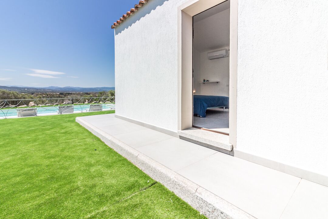 Um edifício moderno e branco com varanda, com vista para um gramado bem cuidado e uma piscina.
