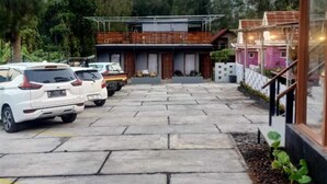Uma área de estacionamento com vários carros, um edifício com varanda de madeira e montanhas ao fundo.