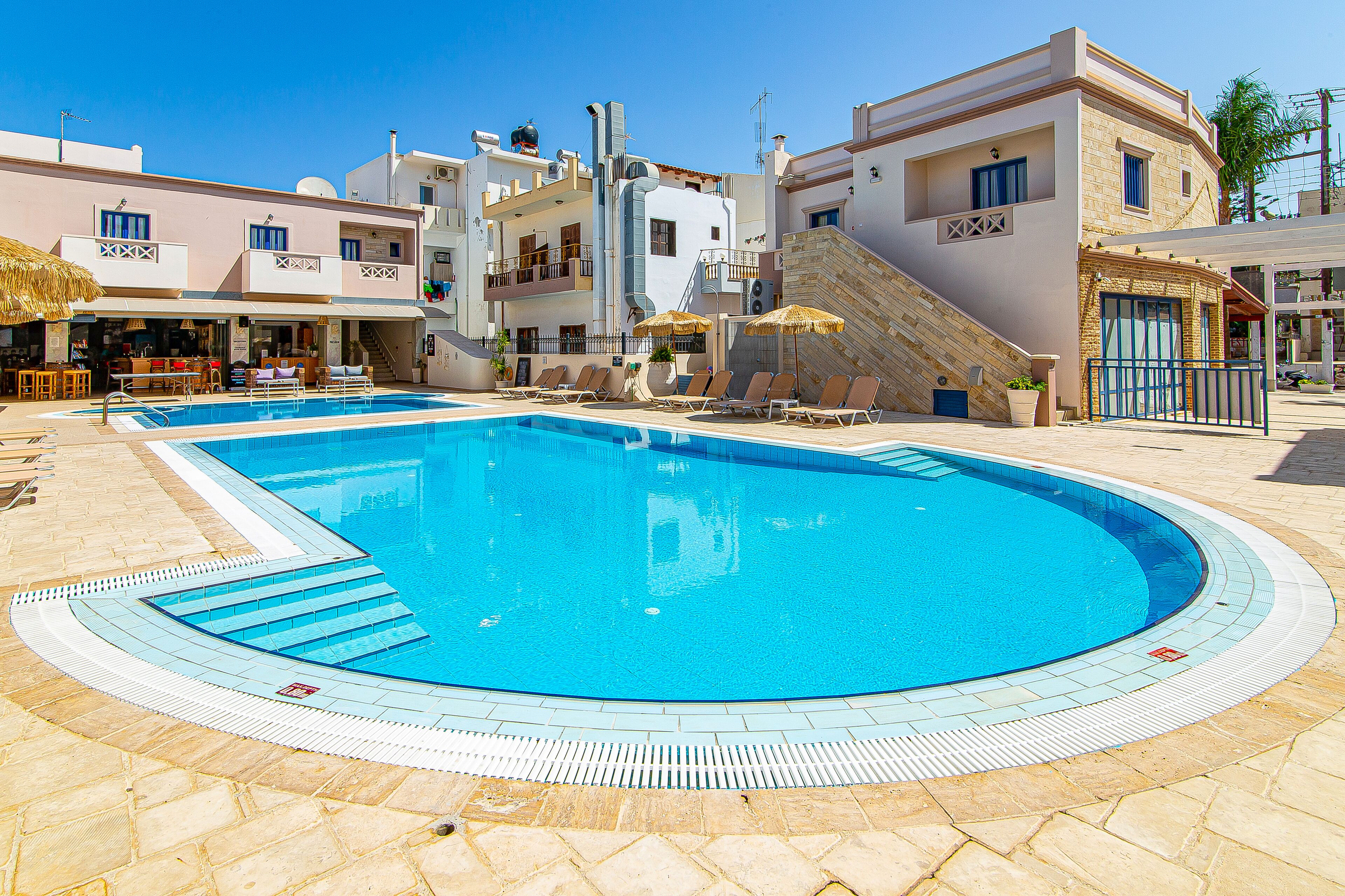 Piscina com espreguiçadeiras e área de bar, rodeada por edifícios com varandas e uma escadaria.