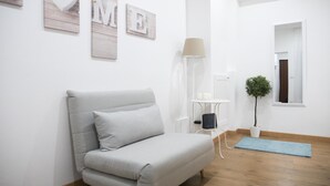 Uma sala de estar moderna com um sofá cinza, uma mesinha com abajur, um vaso de planta e um tapete azul.