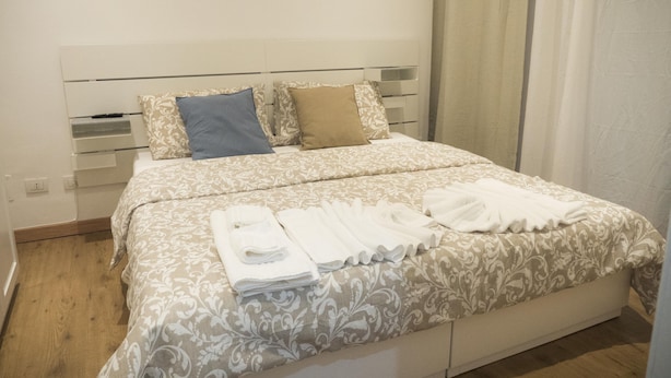 Cama bem arrumada com colcha estampada, duas almofadas e uma toalha dobrada ao lado.