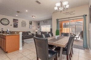 Cozinha moderna com bancada de granito, forno embutido e cafeteira. Há uma sala de jantar com mesa e cadeiras de madeira, e uma sala de estar com sofá e mesa de centro.