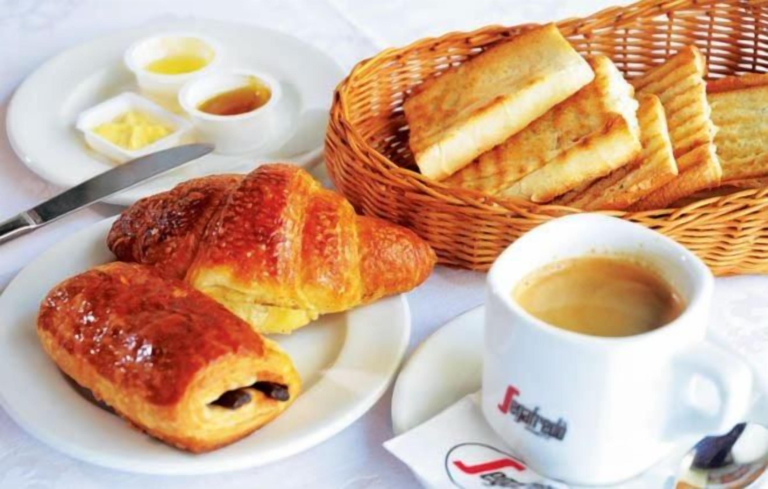 Mesa de café da manhã com croissants, pão e uma xícara de café.