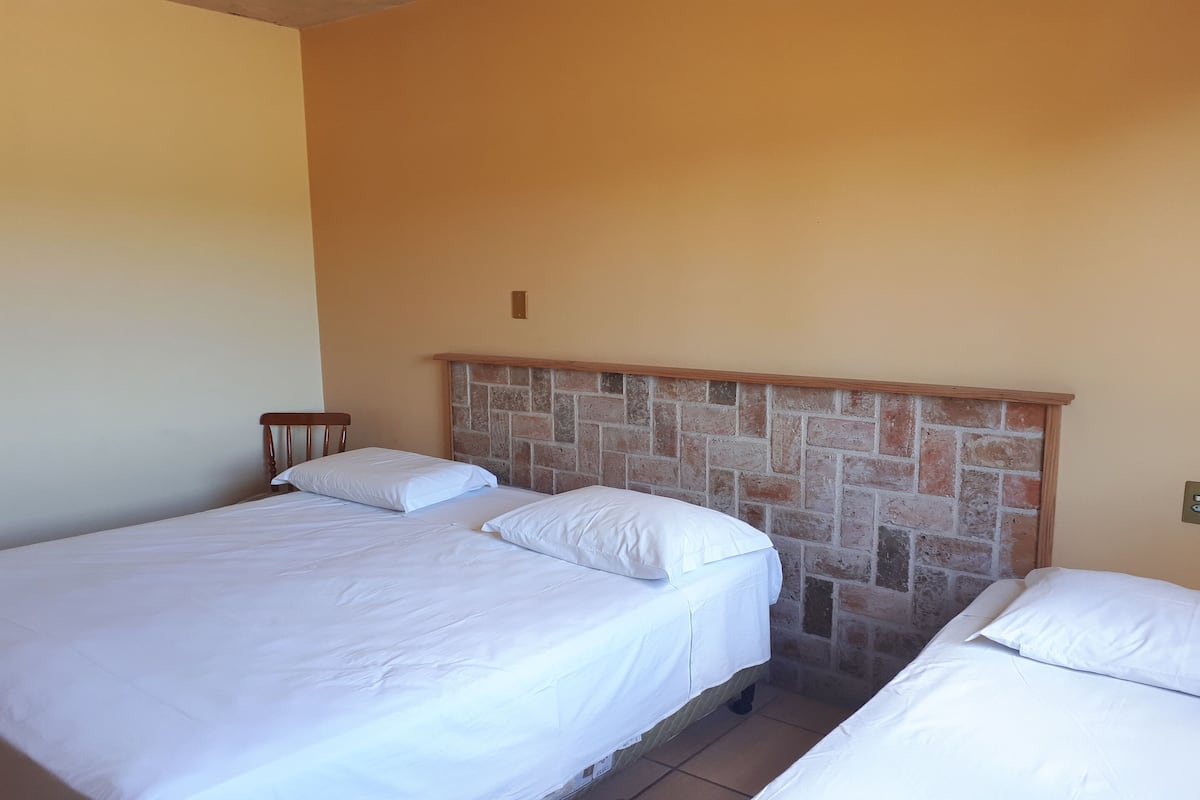 Quarto com duas camas de solteiro, cabeceira com padrão de tijolos e parede lisa.