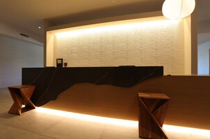 Bancada de recepção com tampo de mármore, painéis laterais de madeira e dois banquinhos de madeira.