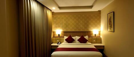 Quarto de hotel com uma cama grande, duas mesas de cabeceira com luminárias, parede estampada e cortina à esquerda.