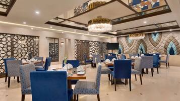 Uma sala de jantar moderna com cadeiras estofadas em azul, lustres e painéis decorativos nas paredes.