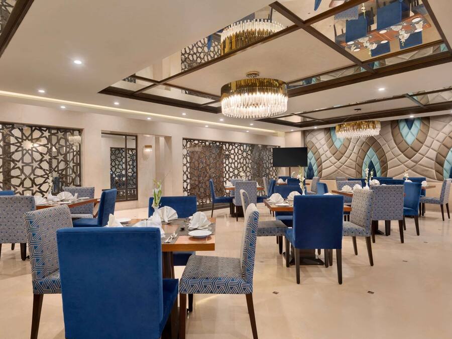 Uma sala de jantar moderna com cadeiras estofadas em azul, lustres e painéis decorativos nas paredes.