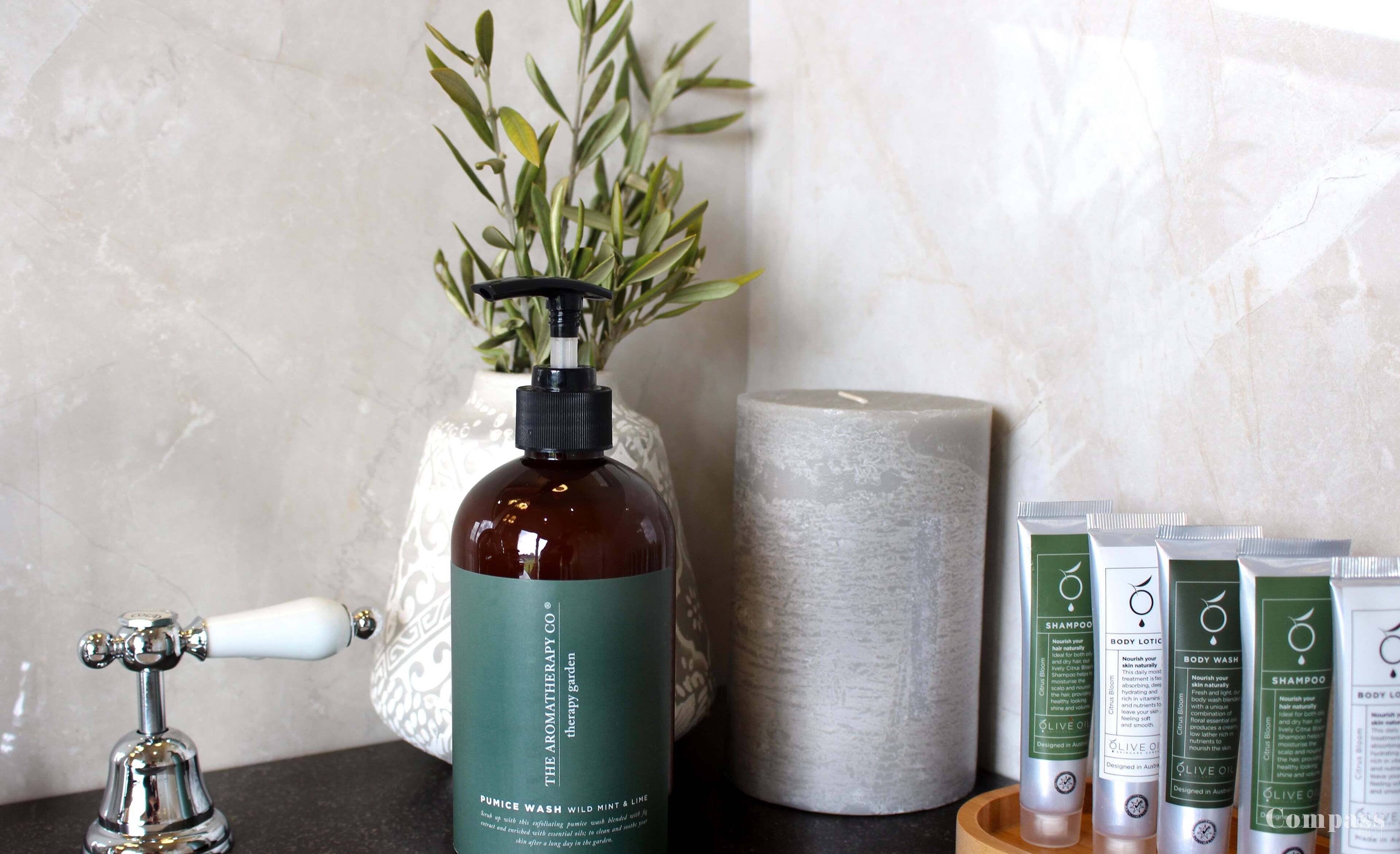 Casa de banho com um frasco de Pumice Wash Wild Mint & Lime, uma toalha branca e um conjunto de produtos de higiene pessoal, incluindo gel de banho e champô.