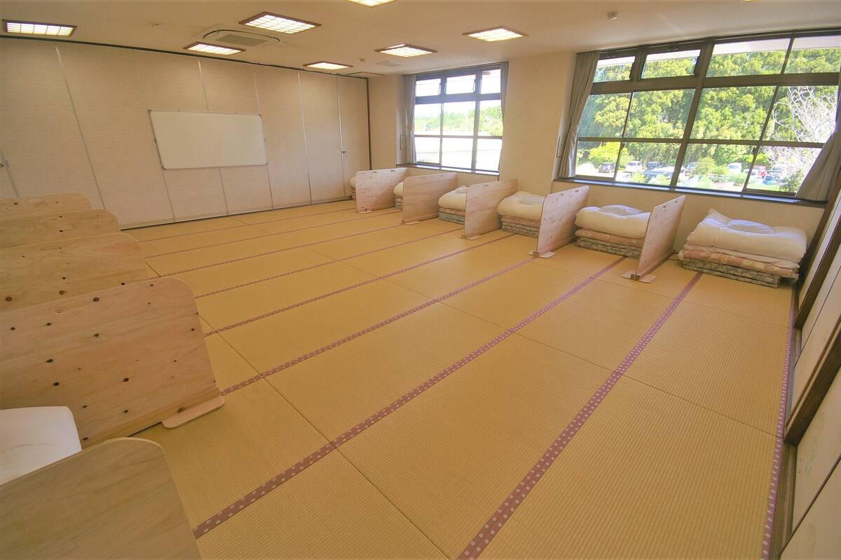 Um espaço com tatames, um quadro branco, bancos de madeira e janelas amplas.