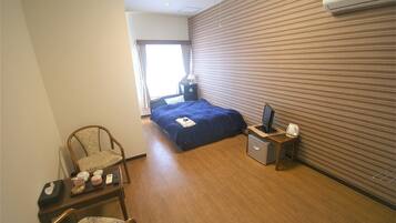 Quarto de hotel com cama, escrivaninha com computador, cadeira, mesa de cabeceira e janela com cortinas.