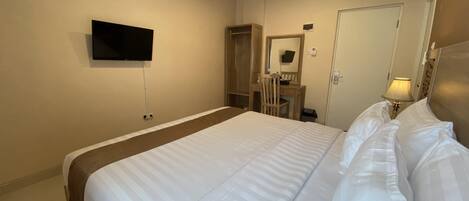 Quarto de hotel com uma cama grande, uma escrivaninha, uma cadeira, uma televisão e uma porta.
