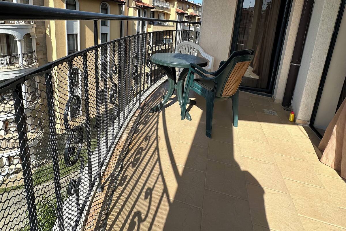 Varanda com mesa e cadeiras, grade de metal e vista para edifícios próximos.