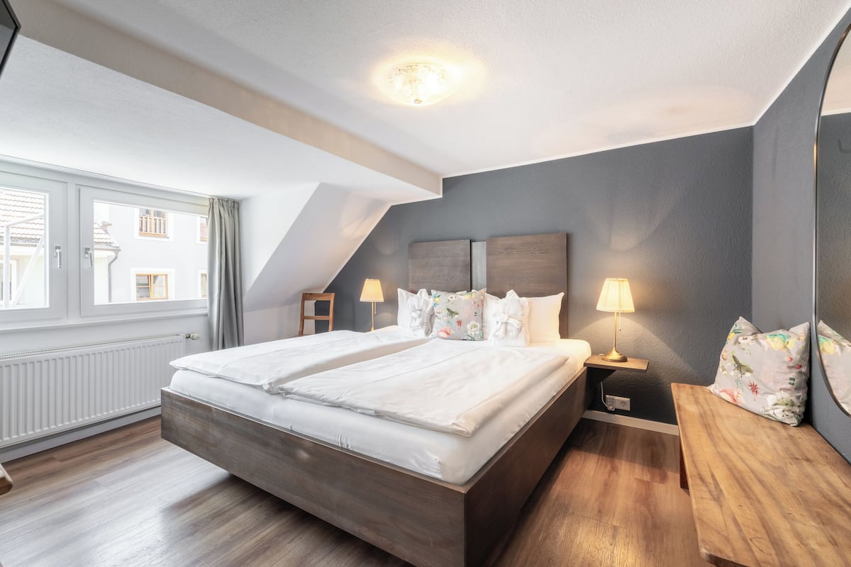 Quarto moderno com uma cama grande, mesa de cabeceira e janela com cortinas.
