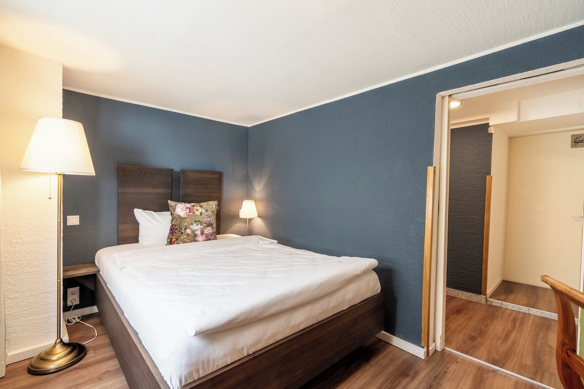 Quarto com uma cama grande, duas luminárias laterais, cabeceira de madeira e um espelho na parede.