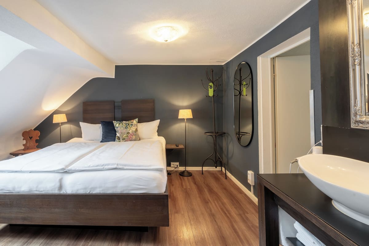 Quarto moderno com cama grande, luminárias de cabeceira, espelho e toucador com pia.