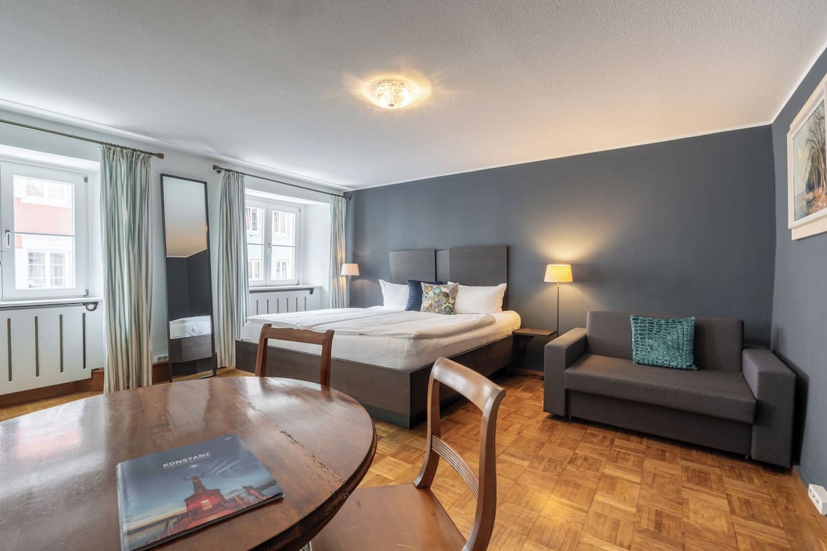 Quarto de hotel com cama, sofá, mesa de jantar e abajur.