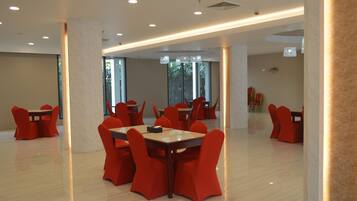 Uma sala de jantar ampla com várias mesas e cadeiras vermelhas, com design moderno, colunas de mármore e iluminação embutida.