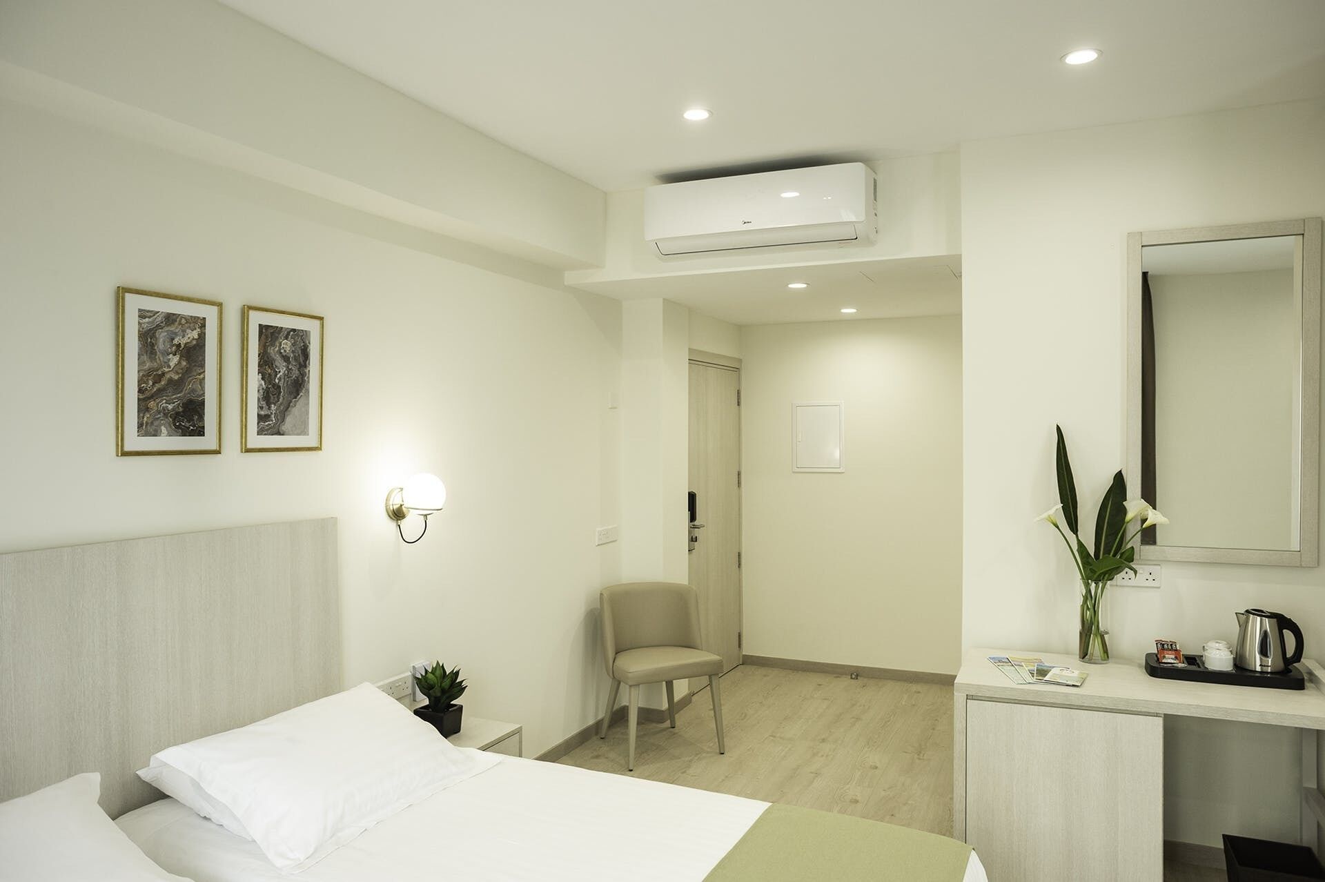 Quarto de hotel com cama, escrivaninha com espelho, cadeira e ar condicionado.