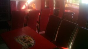 Interior de restaurante com cadeiras e mesas vermelhas, cartazes nas paredes e uma janela que permite entrada de luz natural.