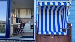 Edifício azul com cozinha, área de jantar e deck de madeira com toldo listrado.