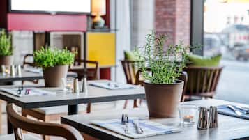 Um restaurante com mesas, cadeiras, plantas em vasos e um aviso do Intercity Hotel.