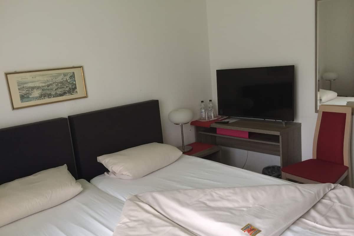 Quarto de hotel com cama, televisão, secretária e cadeira.