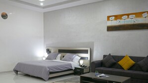 Quarto de hotel moderno com cama, sofá, mesa de centro e um quadro na parede.