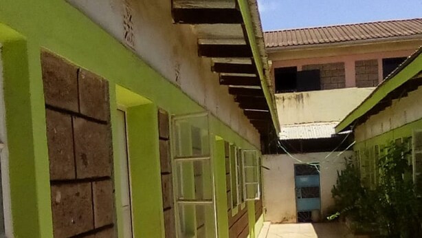 Um corredor com paredes e portas pintadas de verde, que leva a um edifício com telhado de azulejos.