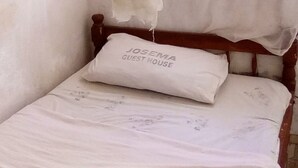 Uma cama de solteiro com colchão branco e travesseiro com a inscrição "JOSEMA GUEST HOUSE".