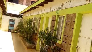 Um corredor estreito com chão de azulejos, paredes pintadas de verde e janelas com persianas de madeira.