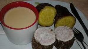 Um prato com uma tigela de sopa, picles e dois rolinhos de carne.