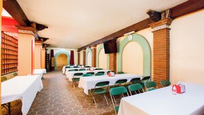 Uma sala de banquetes com várias mesas e cadeiras, piso de azulejos e paredes de tijolo.