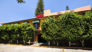 Um hotel com uma placa vermelha chamativa, rodeado por árvores verdes exuberantes e um céu azul límpido.