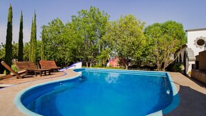 Piscina com borda curva, cercada por um espaço de estar com espreguiçadeiras de madeira e uma mesa pequena.