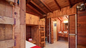 Uma cabana de madeira com cama, uma mesa pequena e banheiro com pia e espelho.