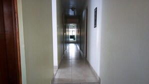 Um corredor comprido e estreito, com chão de azulejos e uma porta de madeira à esquerda.