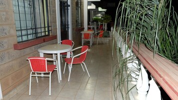 Uma área externa coberta com mesas, cadeiras, plantas em vasos e um muro de pedra.